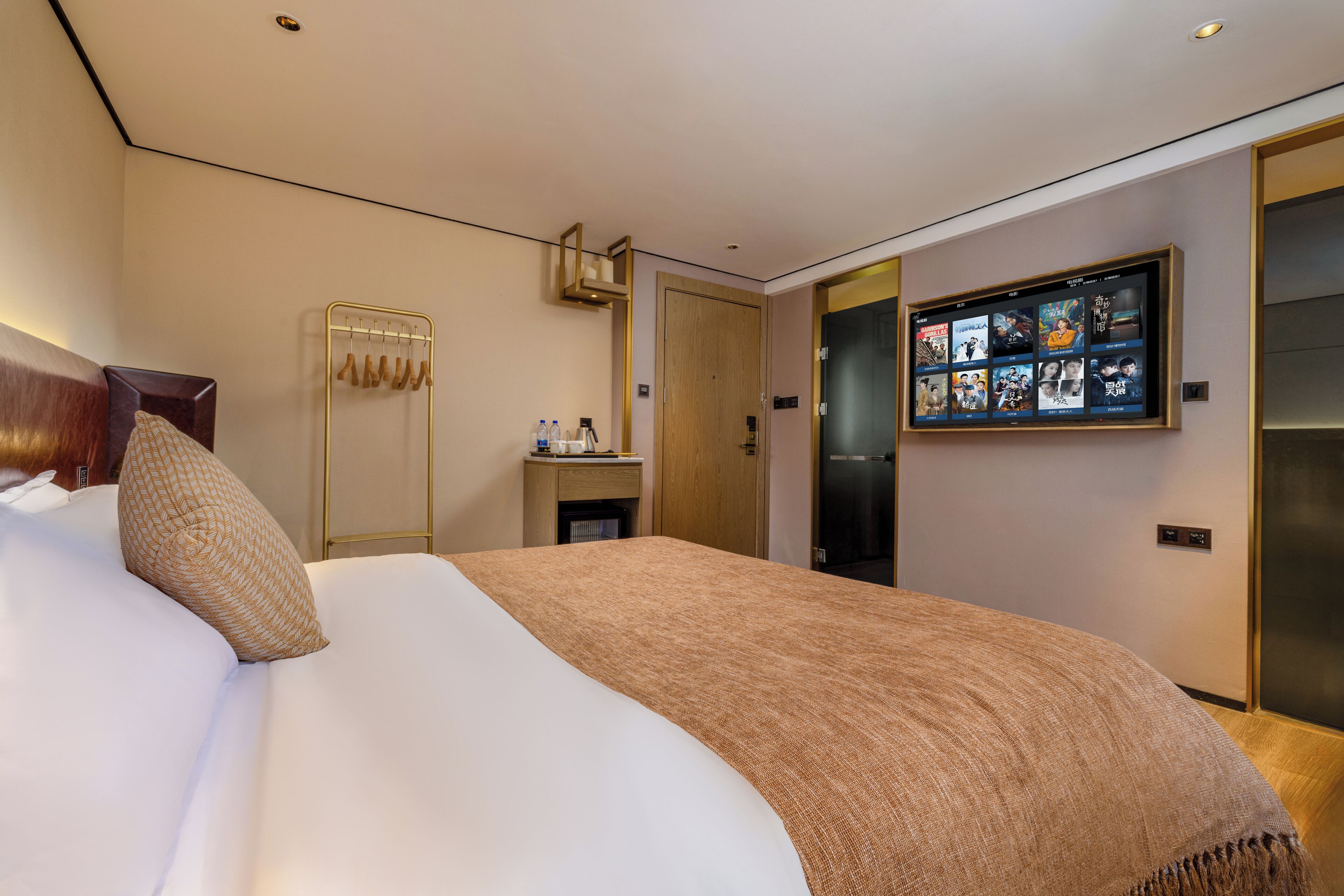 Quarto de hotel com cama, televisão fixada na parede, guarda-roupa de madeira e espelho.