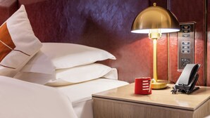 Quarto de hotel com cama bem arrumada, luminária de cabeceira, telefone e painel de controle fixado na parede.