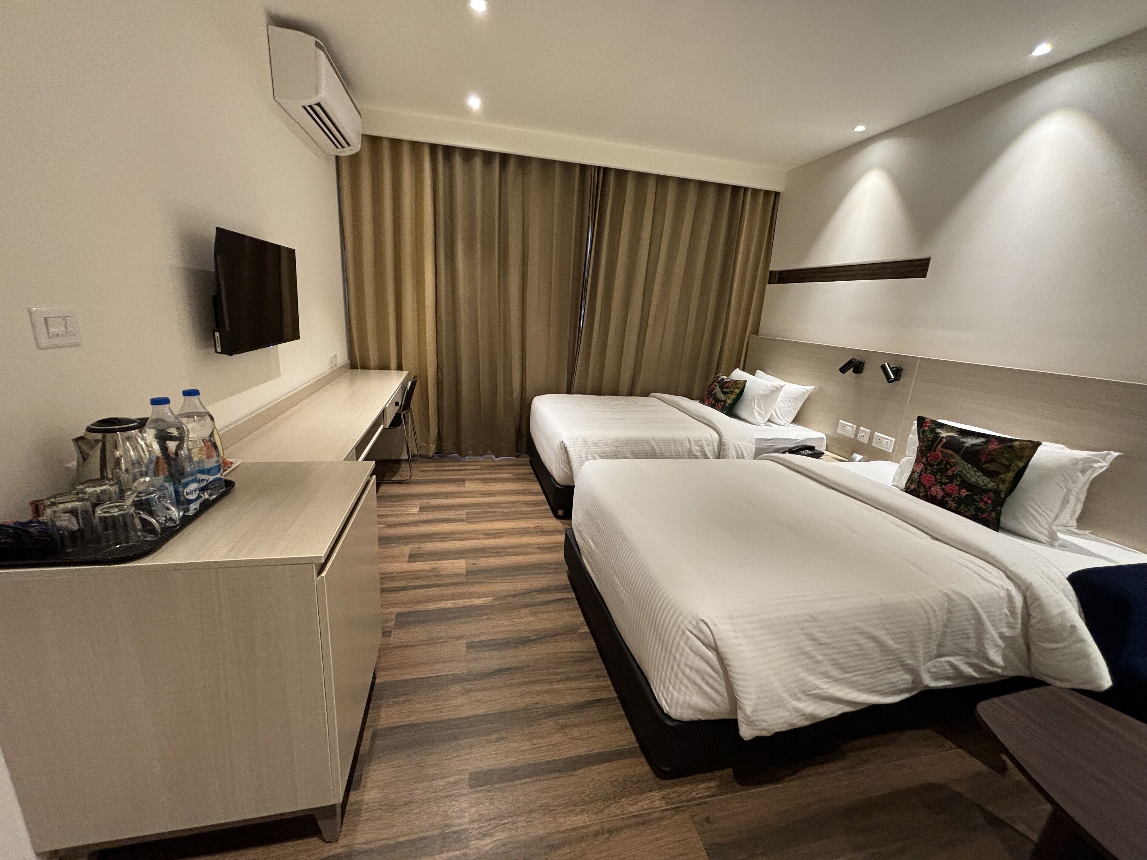 Quarto de hotel com duas camas, uma escrivaninha, televisão e minibar.