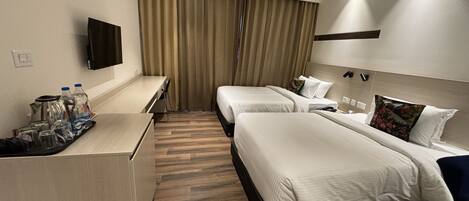 Quarto de hotel com duas camas, uma escrivaninha, televisão e minibar.