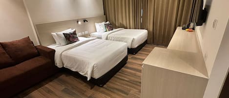 Quarto de hotel com duas camas, um sofá, uma escrivaninha e uma televisão.