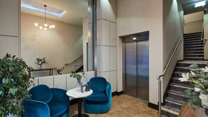 Um lobby moderno com escadaria, balcão de recepção e duas poltronas azuis.