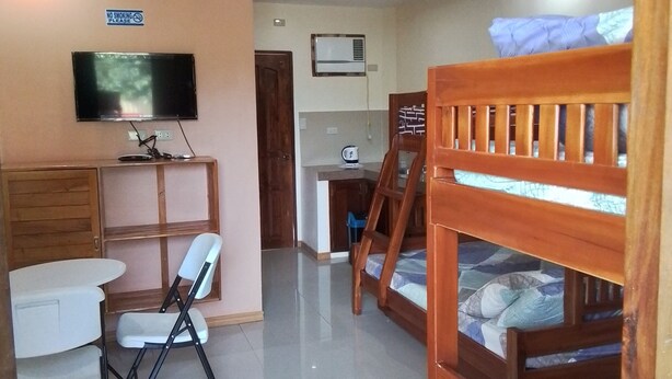 Quarto com beliches, escrivaninha, cadeira, televisão e placa indicando proibição de fumar.