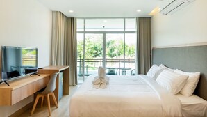 Quarto de hotel com cama, escrivaninha com televisão e vista para o verde lá fora.
