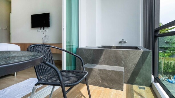 Quarto de hotel moderno com varanda envidraçada, televisão preta montada na parede, uma cadeira preta e uma banheira de pedra.