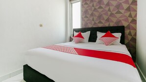 Uma cama bem arrumada com colcha vermelha e branca, cabeceira preta e dois travesseiros vermelhos.