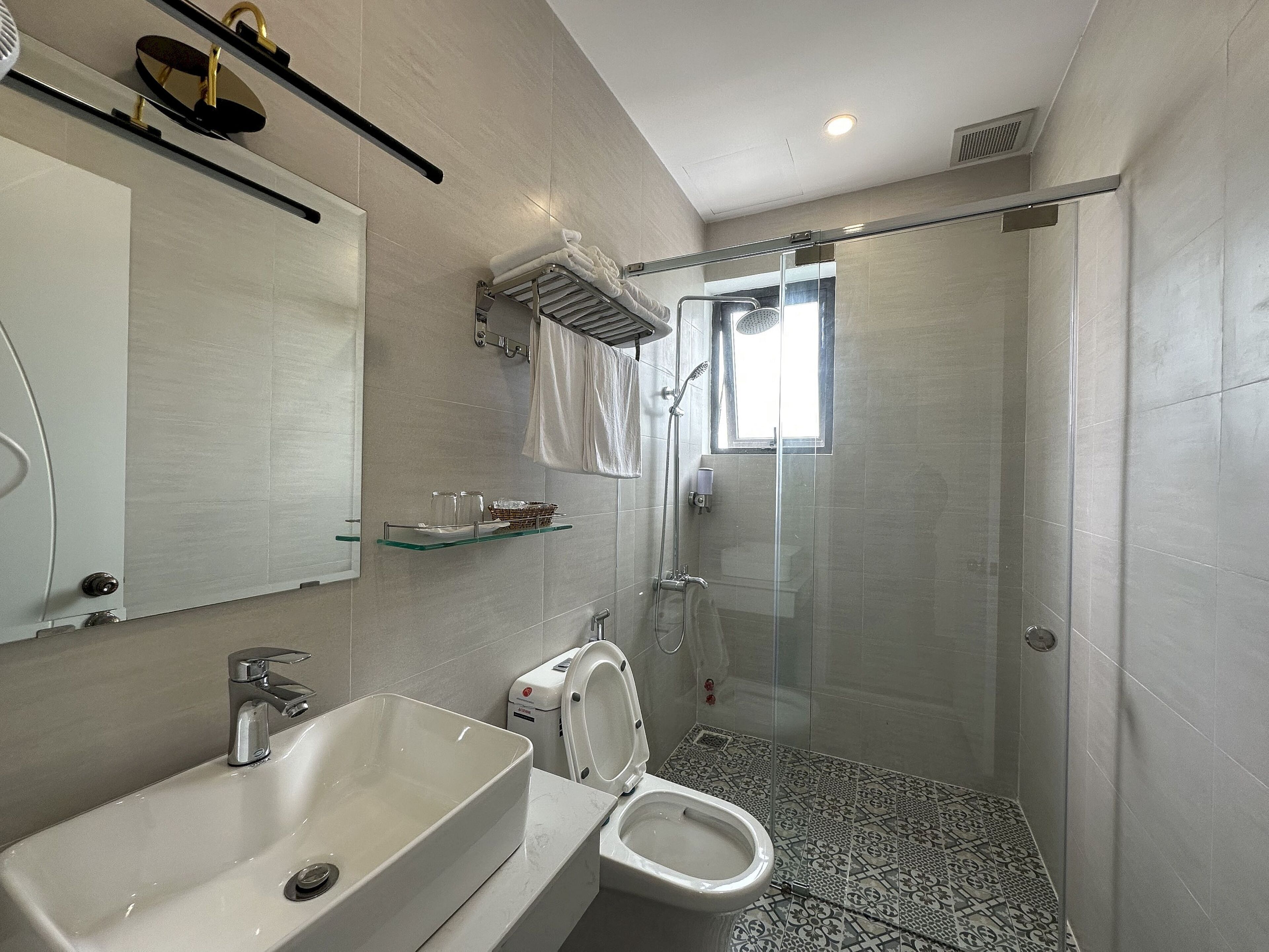Casa de banho moderna com uma grande pia, sanita e zona de duche com divisória de vidro.