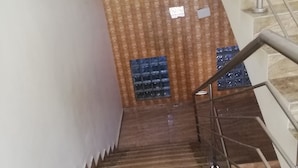 Uma escadaria de mármore com guarda-corpos de metal que leva a um quarto com papel de parede estampado e parede revestida de azulejos.