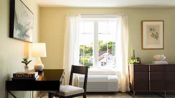 Quarto com escrivaninha, cadeira, luminária, livros, radiador e janela com cortinas.