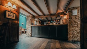 Uma área de bar com vigas de madeira, paredes de pedra e balcão com garrafas.