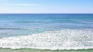 Visão nítida de uma praia com águas calmas e um nadador ao longe.
