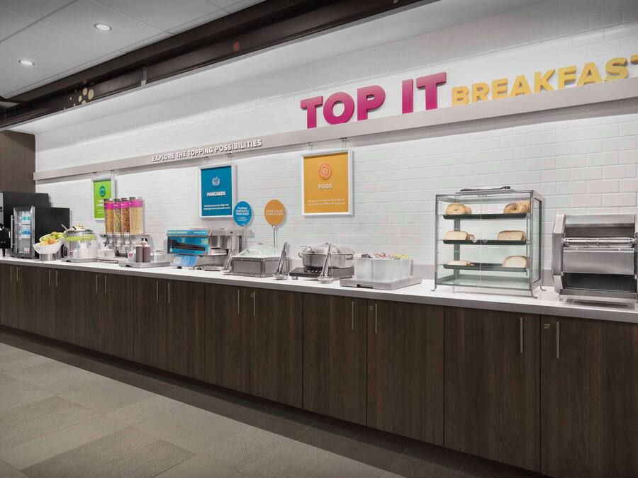 Uma mesa de pequeno-almoço com um letreiro a dizer "TOP IT BREAKFAST" e vários alimentos em exposição.