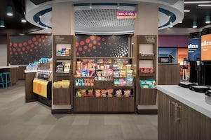 Quiosque de lanches com diversos alimentos e bebidas embalados, placa indicando mercado 24 horas e logotipo da Hilton, indicando serviços de hotel próximos.