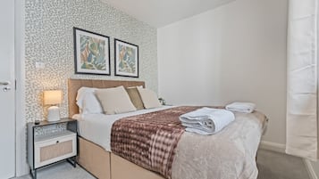Quarto de hotel com cama, mesa de cabeceira, abajur e duas fotografias emolduradas na parede.