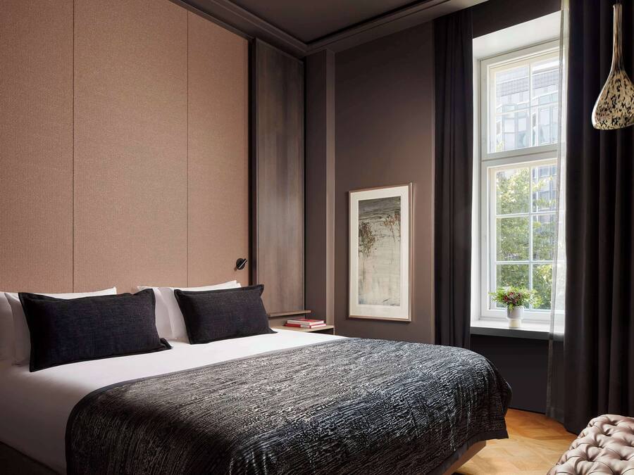 Quarto de hotel moderno com uma cama grande, mesa de cabeceira, obra de arte emoldurada e uma janela com cortinas.