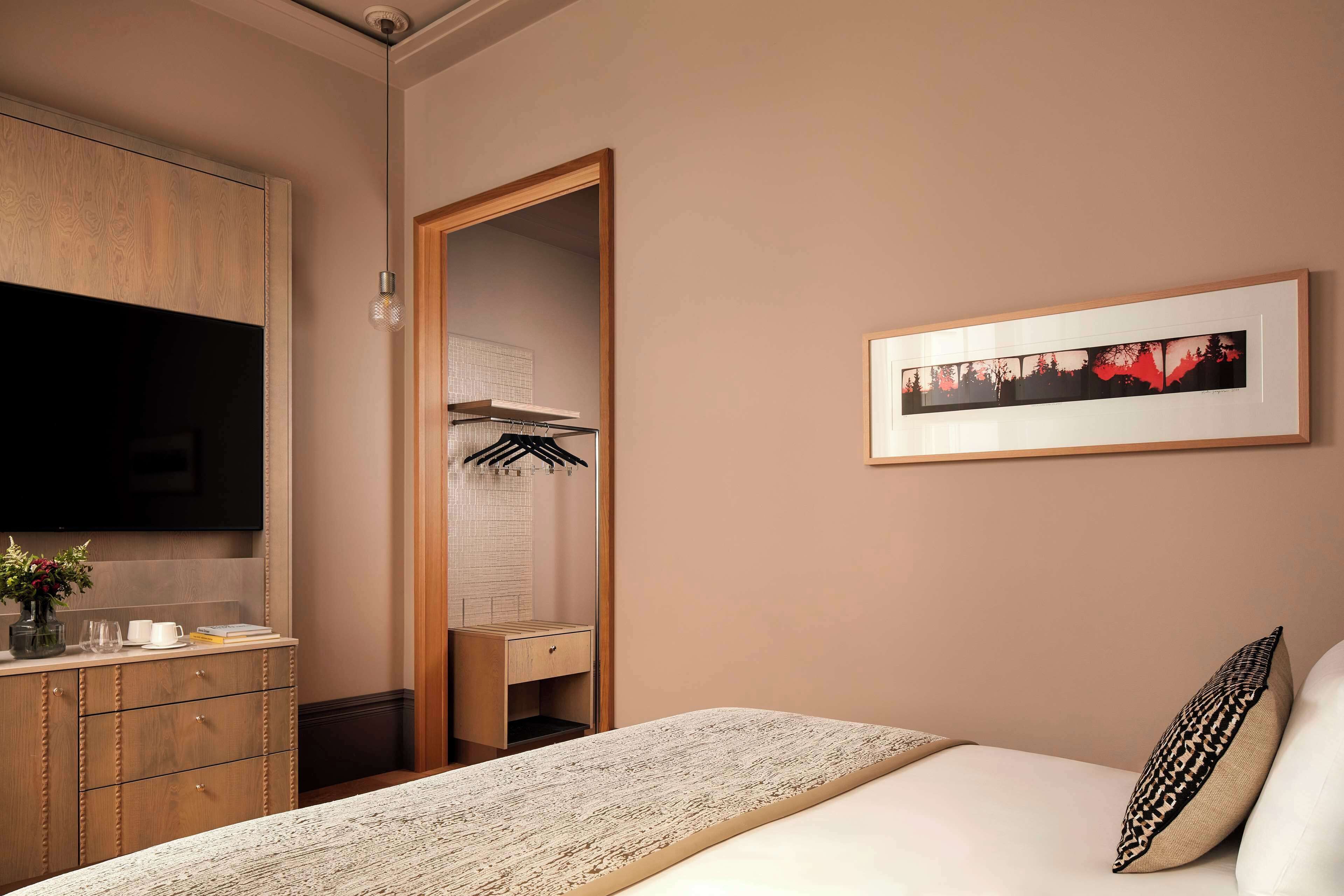 Quarto de hotel com uma cama, penteadeira, televisão, quadro emoldurado e um armário.