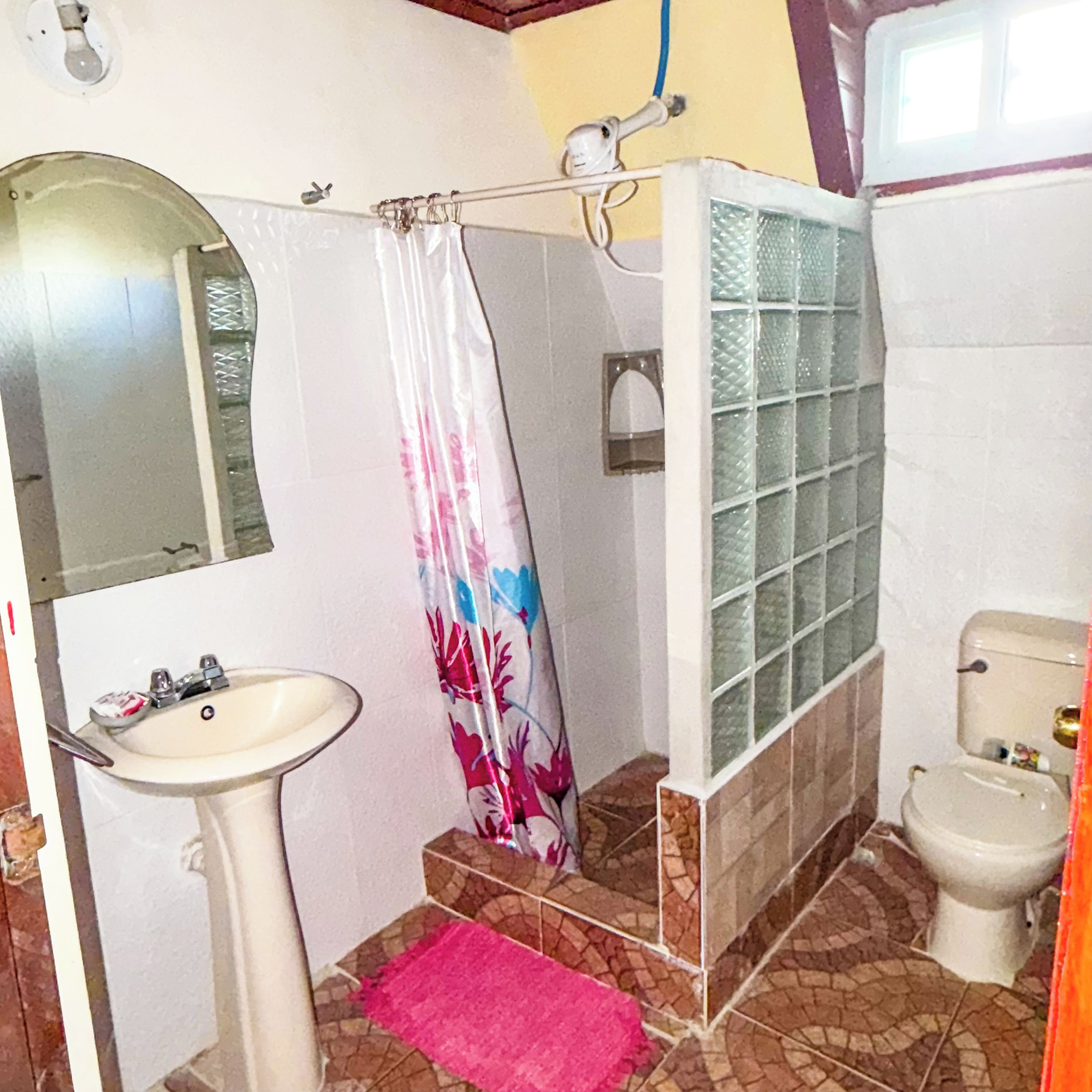 Casa de banho com lavatório, sanita e chuveiro, com espelho.