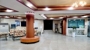 Um hall amplo com um pilar central de madeira, área de estar com cadeiras estampadas com flores e um balcão de recepção.