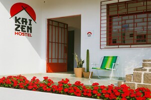 Um hostel com fachada vermelha e branca, uma entrada em estilo japonês tradicional e uma cadeira listrada de verde do lado de fora.