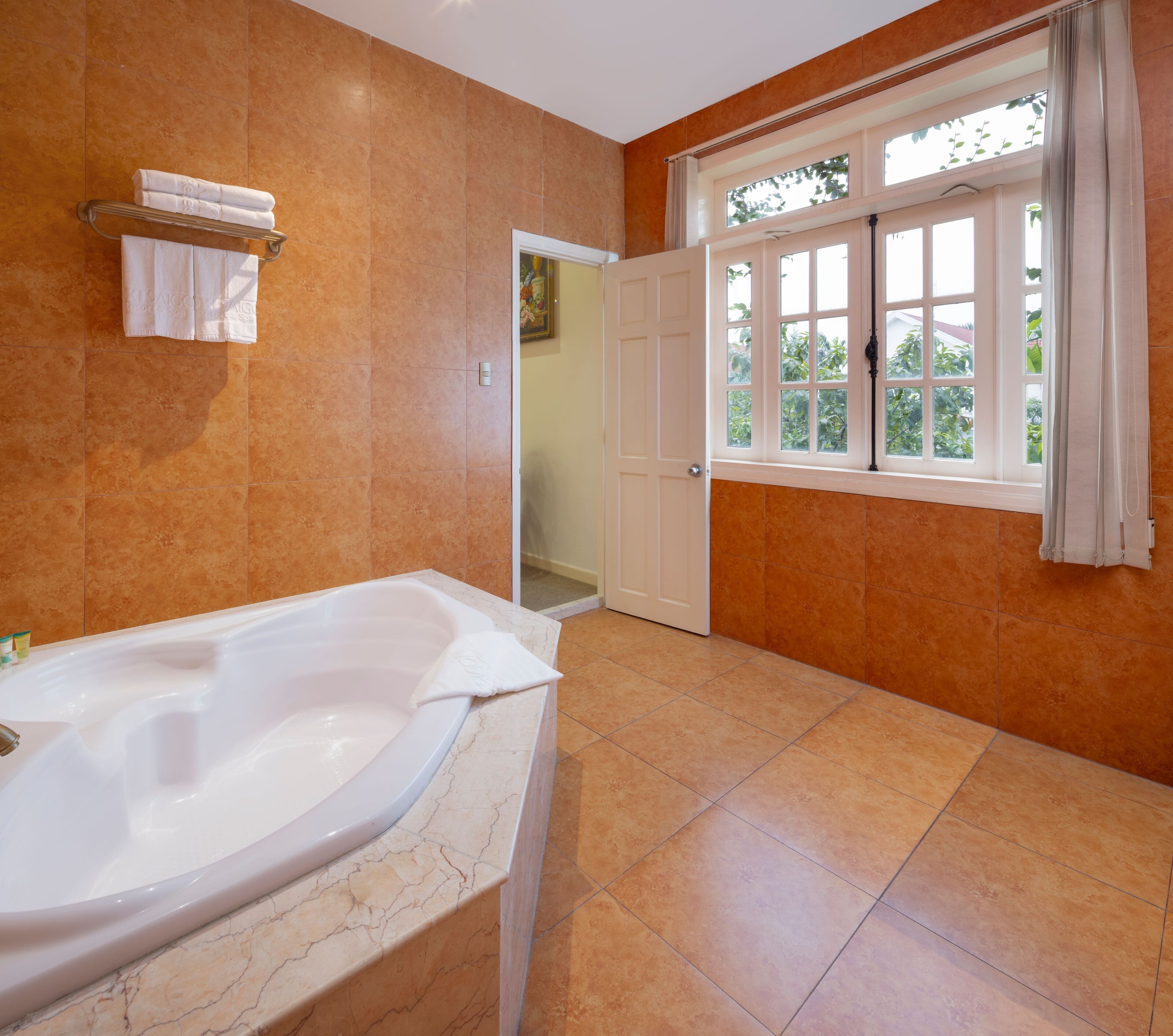 Um banheiro com uma banheira grande, um porta-toalhas com toalhas dobradas e uma janela com cortinas.