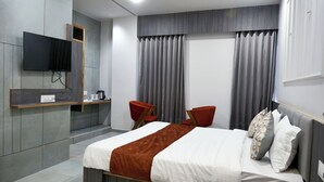 Quarto de hotel moderno com uma cama grande, duas cadeiras vermelhas, uma TV de tela plana na parede e cortinas cinzentas.