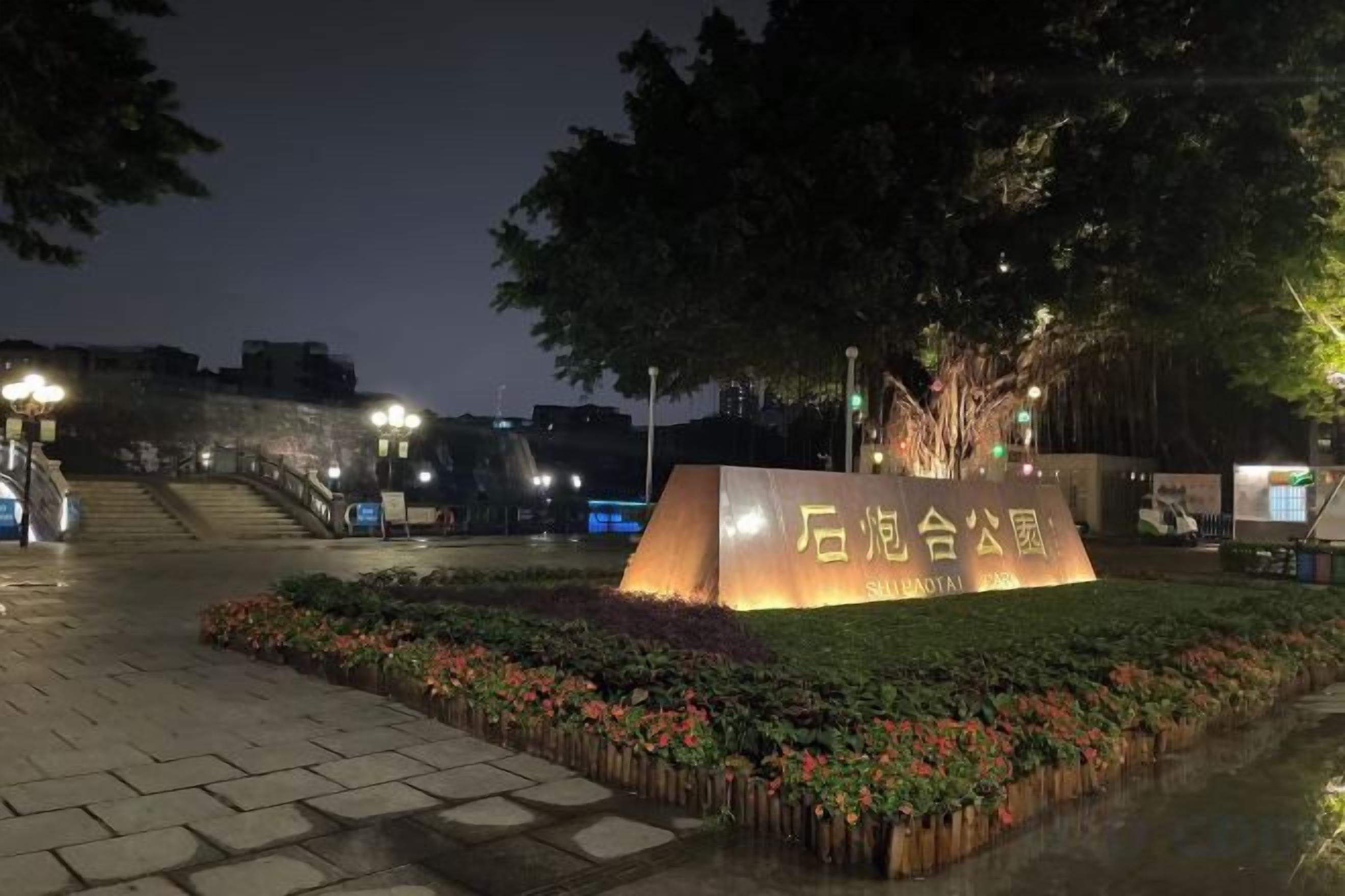 Entrada bem iluminada com um caminho de pedra que leva a uma área ajardinada e uma placa.