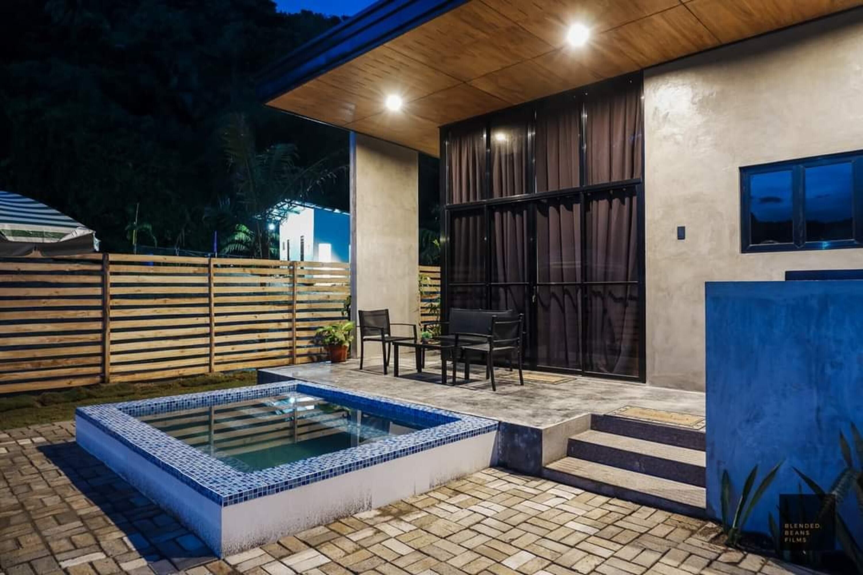 Uma área de piscina moderna ao ar livre com estrutura de vidro, deck de madeira e assentos.