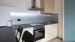 Uma cozinha moderna com coifa de aço inoxidável, armários de madeira, bancada preta e forno embutido.
