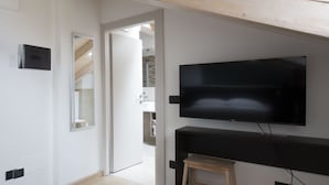 Uma sala de estar moderna com uma TV de tela plana na parede, um banquinho de madeira e uma escada que leva a um andar superior.
