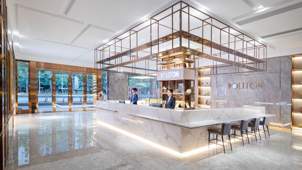 Um hall de hotel moderno com uma recepção de mármore, divisória de vidro e vista para o exterior.