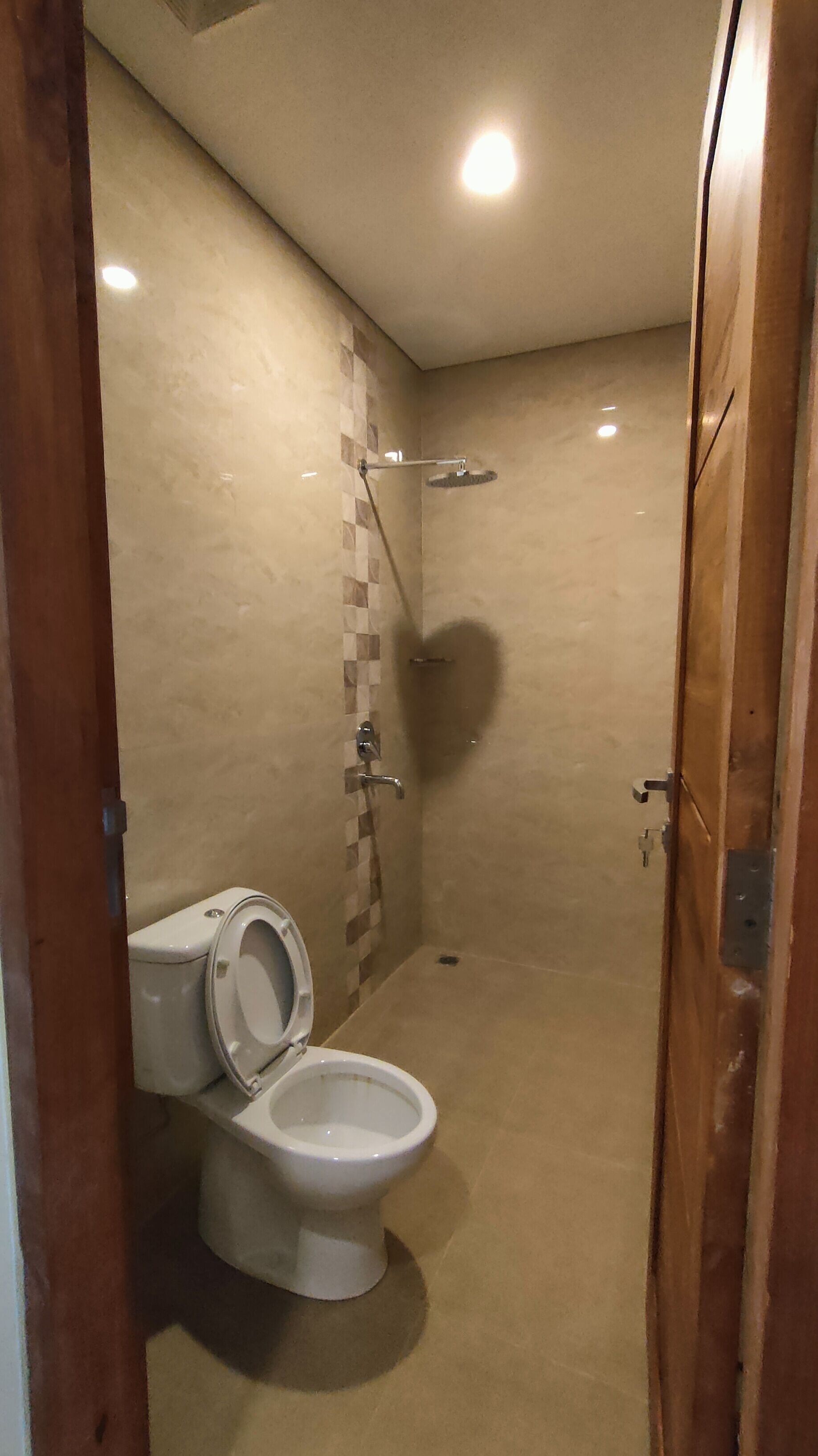 Casa de banho pequena e compacta, com sanita, chuveiro e parede revestida a azulejos.
