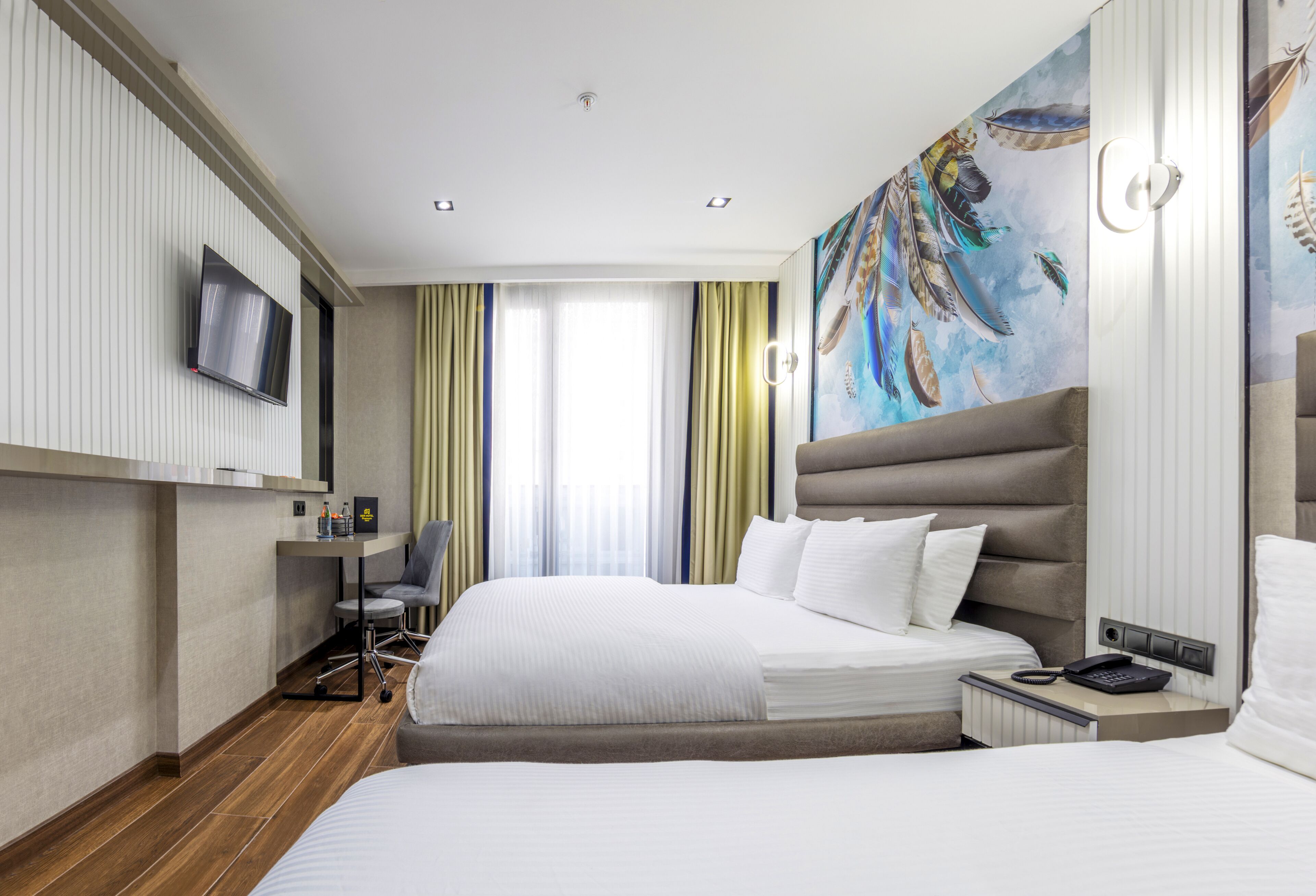 Quarto de hotel com uma cama grande, uma escrivaninha com cadeira, uma televisão e um quadro na parede.