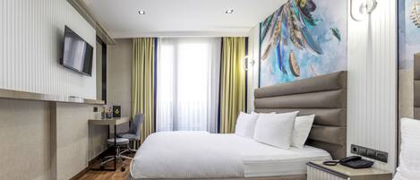 Quarto de hotel com uma cama grande, uma escrivaninha com cadeira, uma televisão e um quadro na parede.