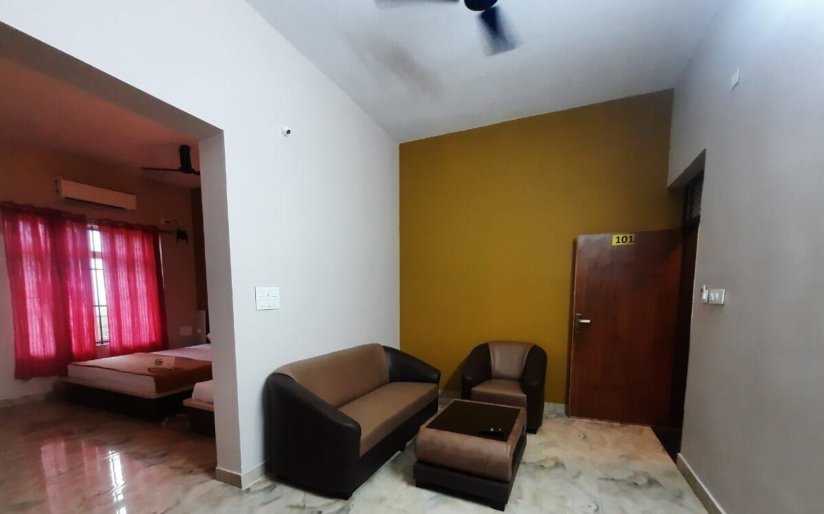 Uma sala de estar com sofá, poltrona e um banquinho, um ventilador de teto e uma porta com o número 101.