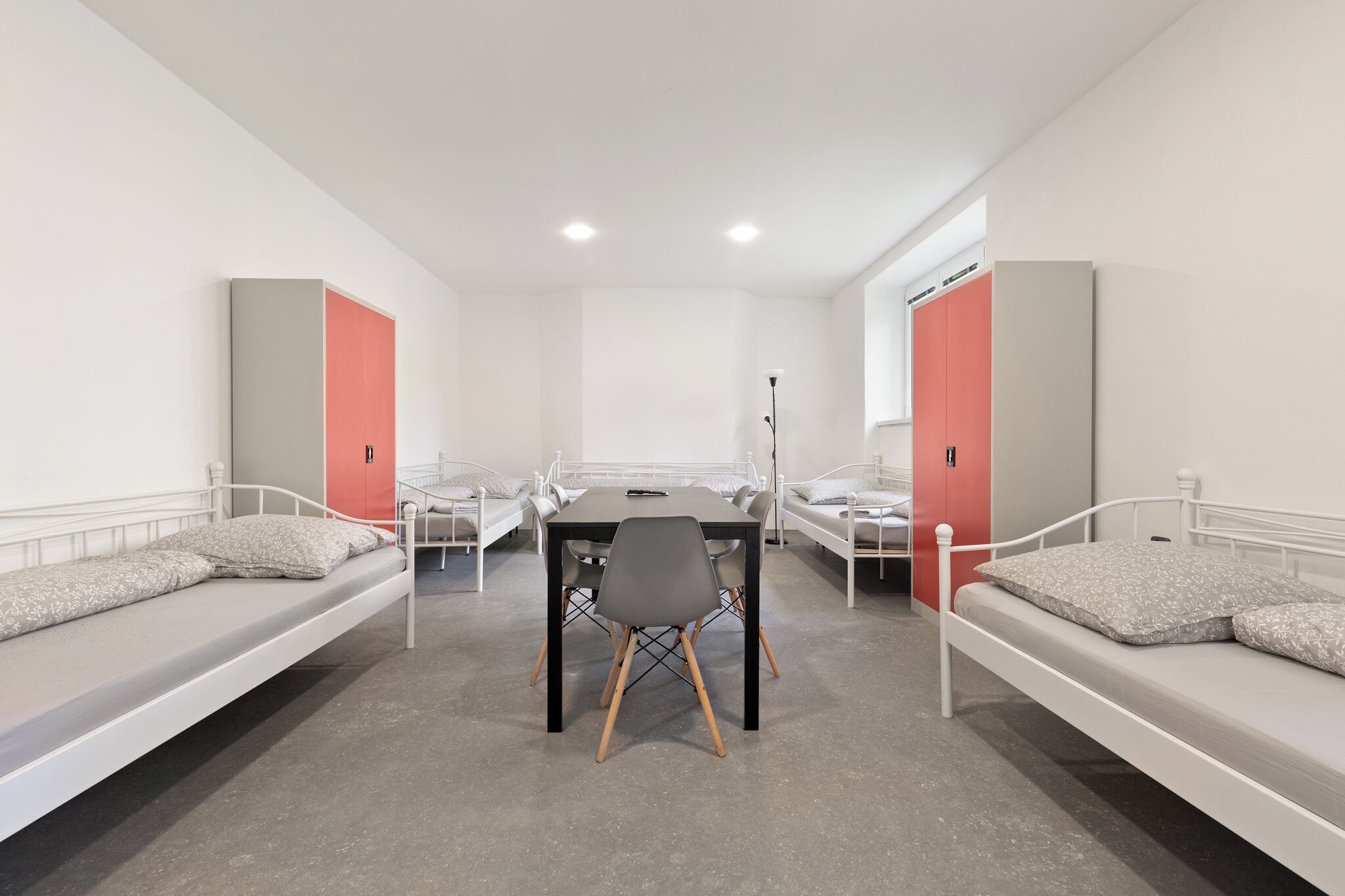 Quarto em dormitório com duas camas de solteiro, uma mesinha e uma cadeira.
