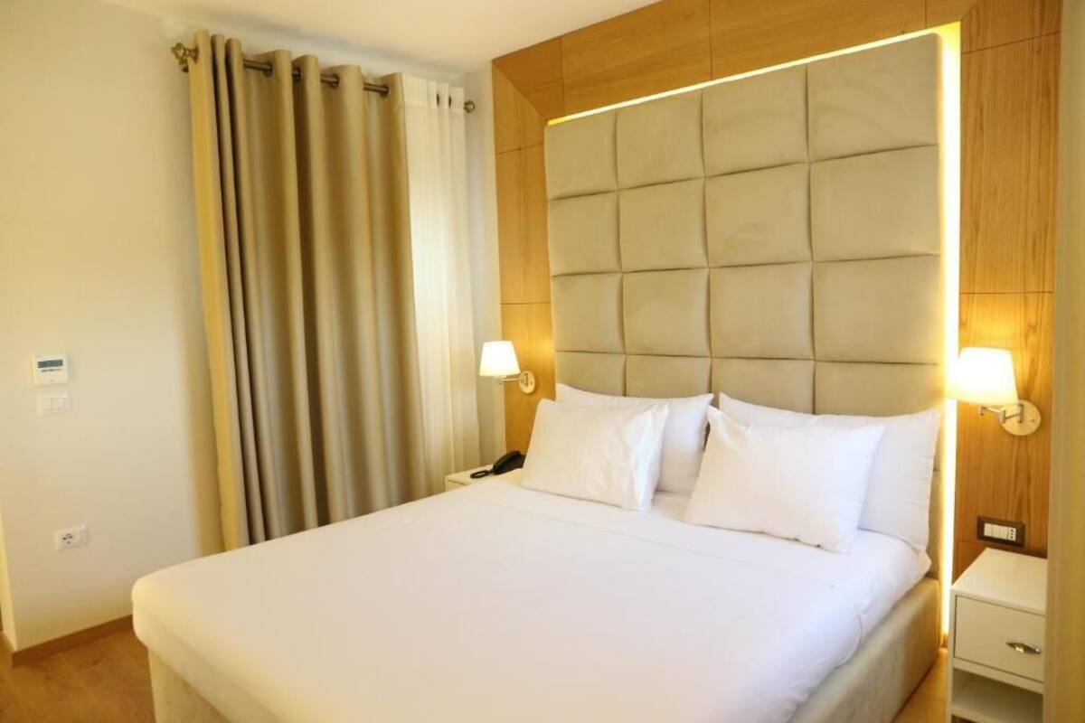 Quarto de hotel com uma cama grande, duas mesas de cabeceira, uma cabeceira e cortinas.