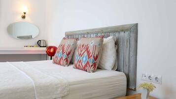 Cama bem arrumada com almofadas estampadas, mesa de cabeceira com abajur e espelho fixado na parede.
