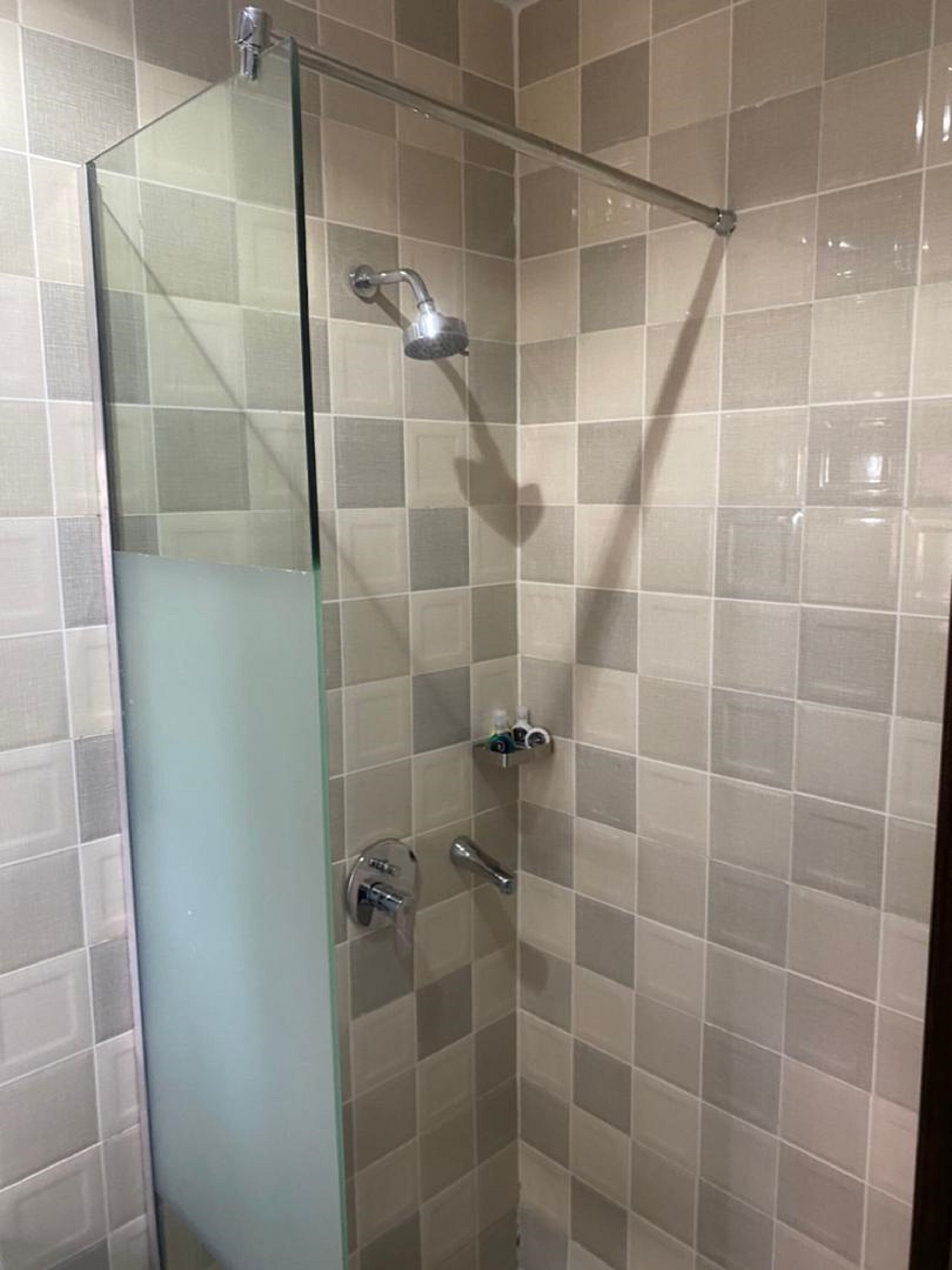 Um chuveiro com paredes de vidro, um chuveiro manual e uma torneira fixada na parede.