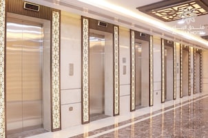 Um corredor de hotel com vários elevadores, cada um com um painel decorativo e um visor digital acima das portas.