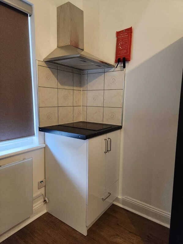 Cozinha compacta com bancada preta, armários brancos e coifa de aço inoxidável.