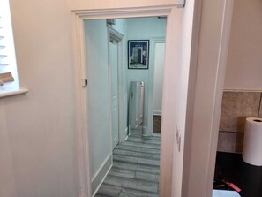 Um corredor estreito com piso de madeira, paredes brancas e uma porta que dá para outro cômodo.
