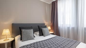 Uma cama bem arrumada com um cobertor xadrez, dois travesseiros e uma luminária de cabeceira em uma mesa de cabeceira branca.