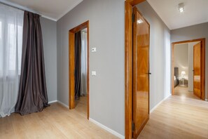 Um corredor com piso de madeira, paredes cinzentas e uma porta que dá para outro quarto.