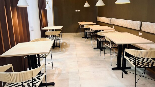 Um restaurante moderno com várias mesas e cadeiras, painéis de madeira numa parede e iluminação pendente.