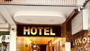 Entrada de hotel com design moderno, destacando fachada de vidro, um sofá de couro no interior e uma placa com a inscrição "HOTEL".