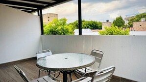 Um alpendre coberto com uma mesa redonda de vidro e quatro cadeiras de metal.