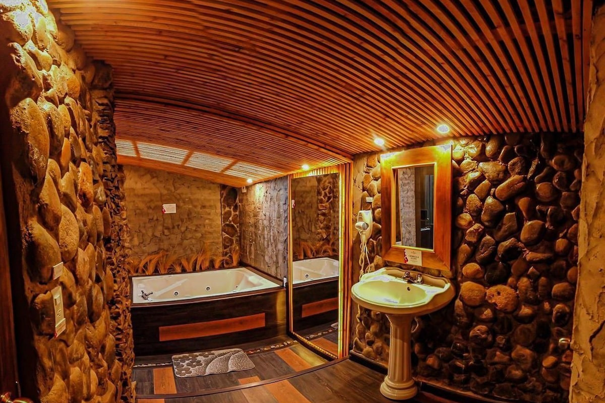 Um quarto de spa com parede de pedra, piso de madeira, uma banheira grande e uma pia.