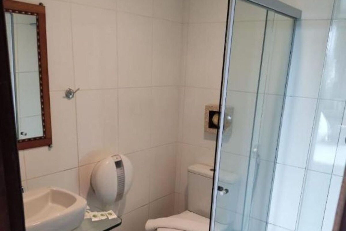 Casa de banho com cabine de duche em vidro, sanita, lavatório e um contentor de lixo.