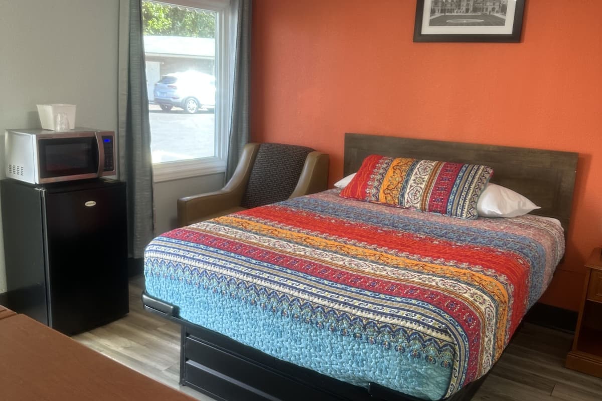 Quarto de hotel com cama, escrivaninha, cadeira, micro-ondas e frigorífico.
