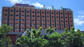 Um hotel com uma placa grande, vários andares e área verde ao redor.